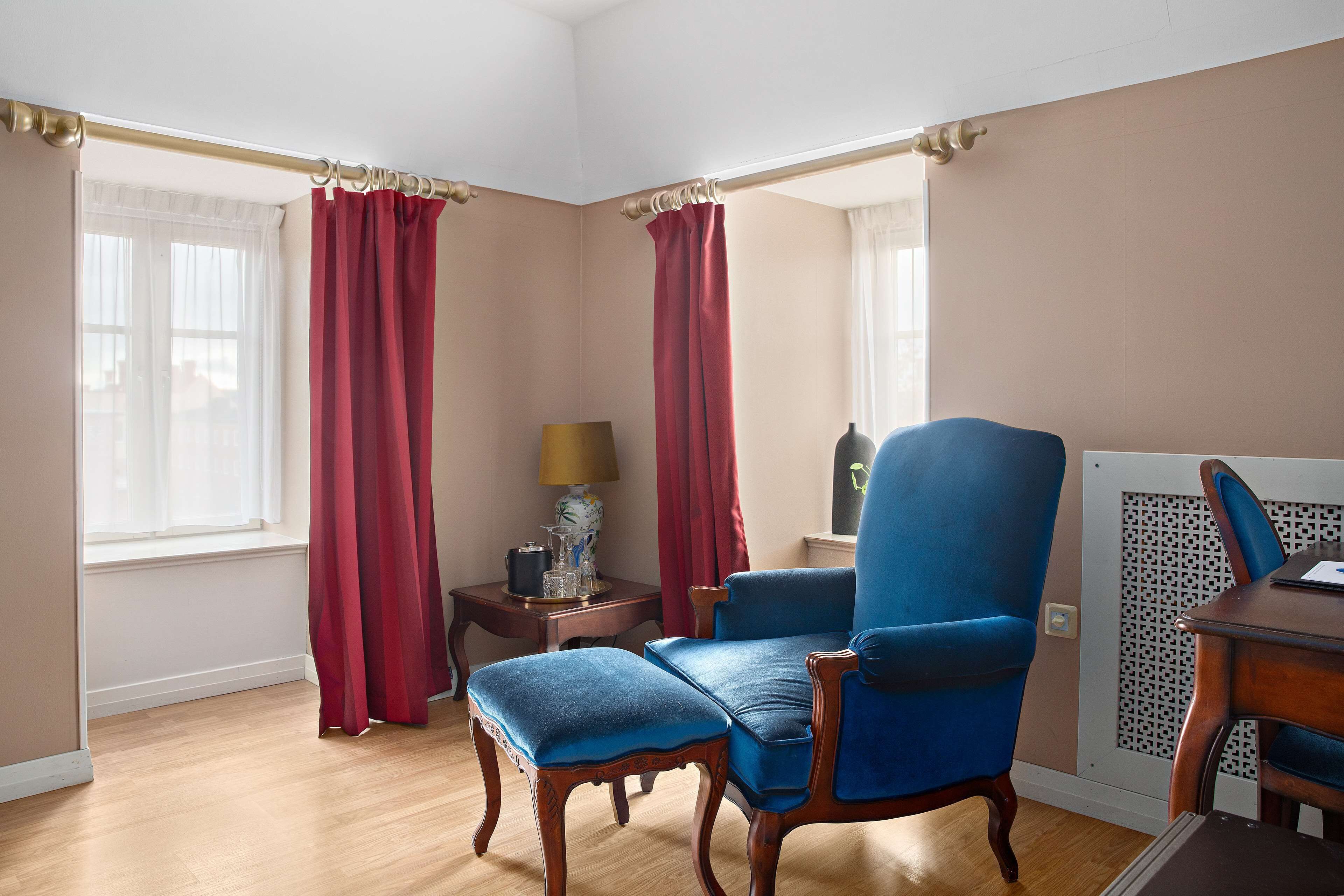 Um quarto com duas poltronas azuis, uma mesa de madeira com abajur e um radiador.