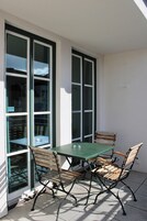 Um pátio externo com mesa e cadeiras, janelas amplas e vista do céu.
