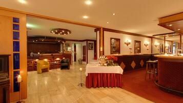Um amplo hall de hotel com área de bar, balcão de recepção e espaço de estar com mesa posta para refeição.