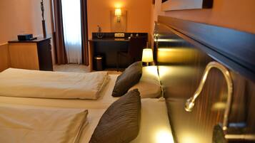 Quarto de hotel com duas camas, uma mesa, uma cadeira, um abajur e uma lixeira.