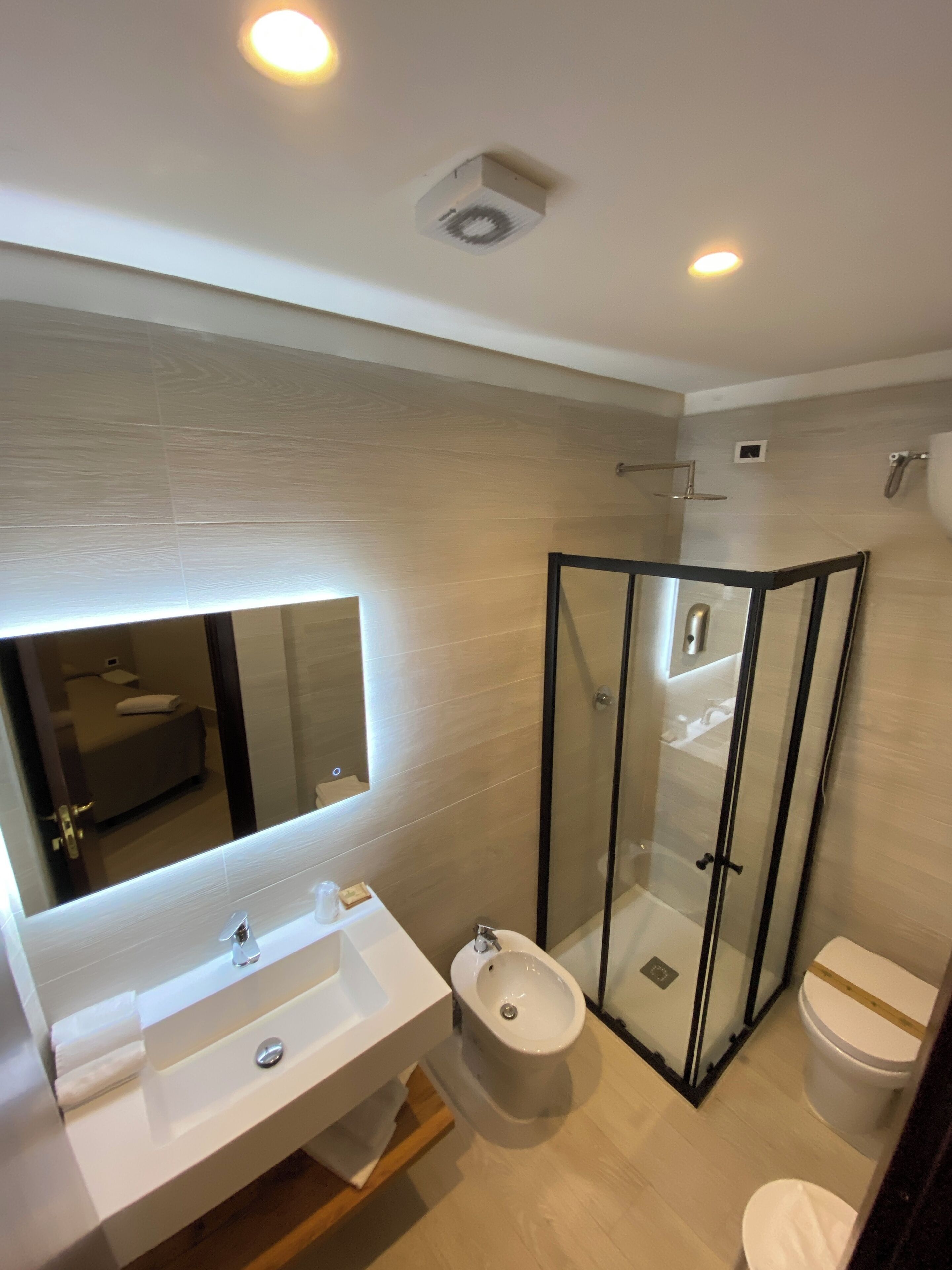 Uma casa de banho moderna com cabine de duche em vidro, uma sanita e uma pia com espelho.