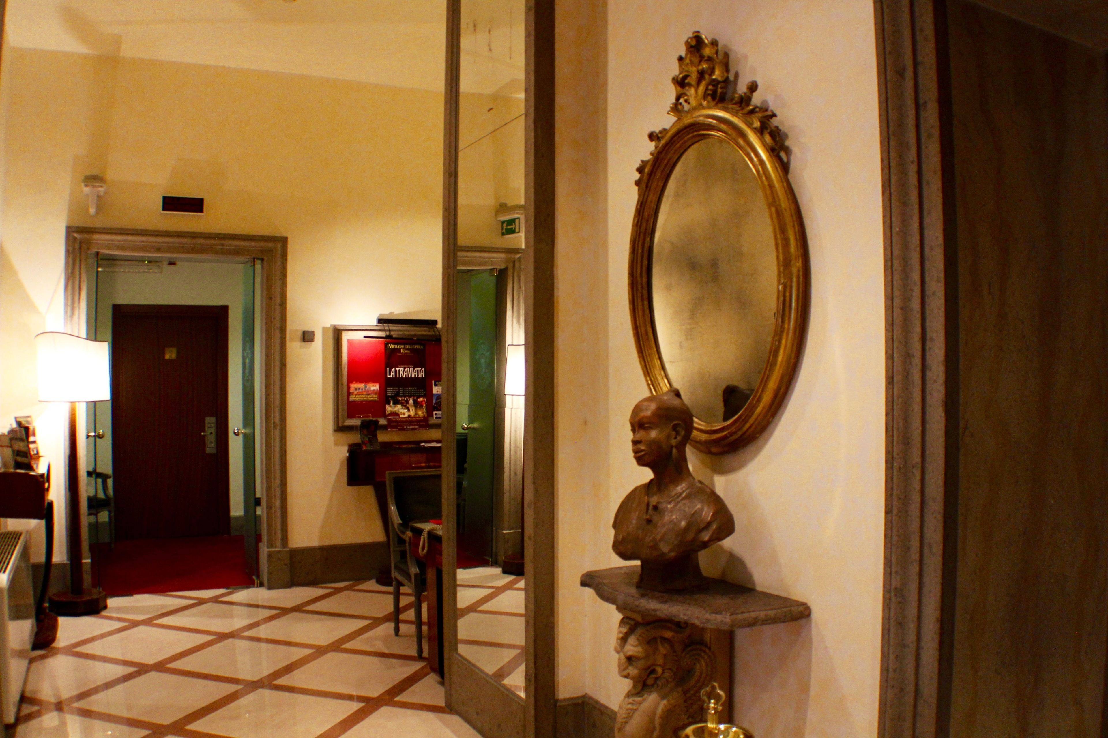 Um saguão de hotel com piso de azulejos, tapete vermelho, uma estátua e um espelho.
