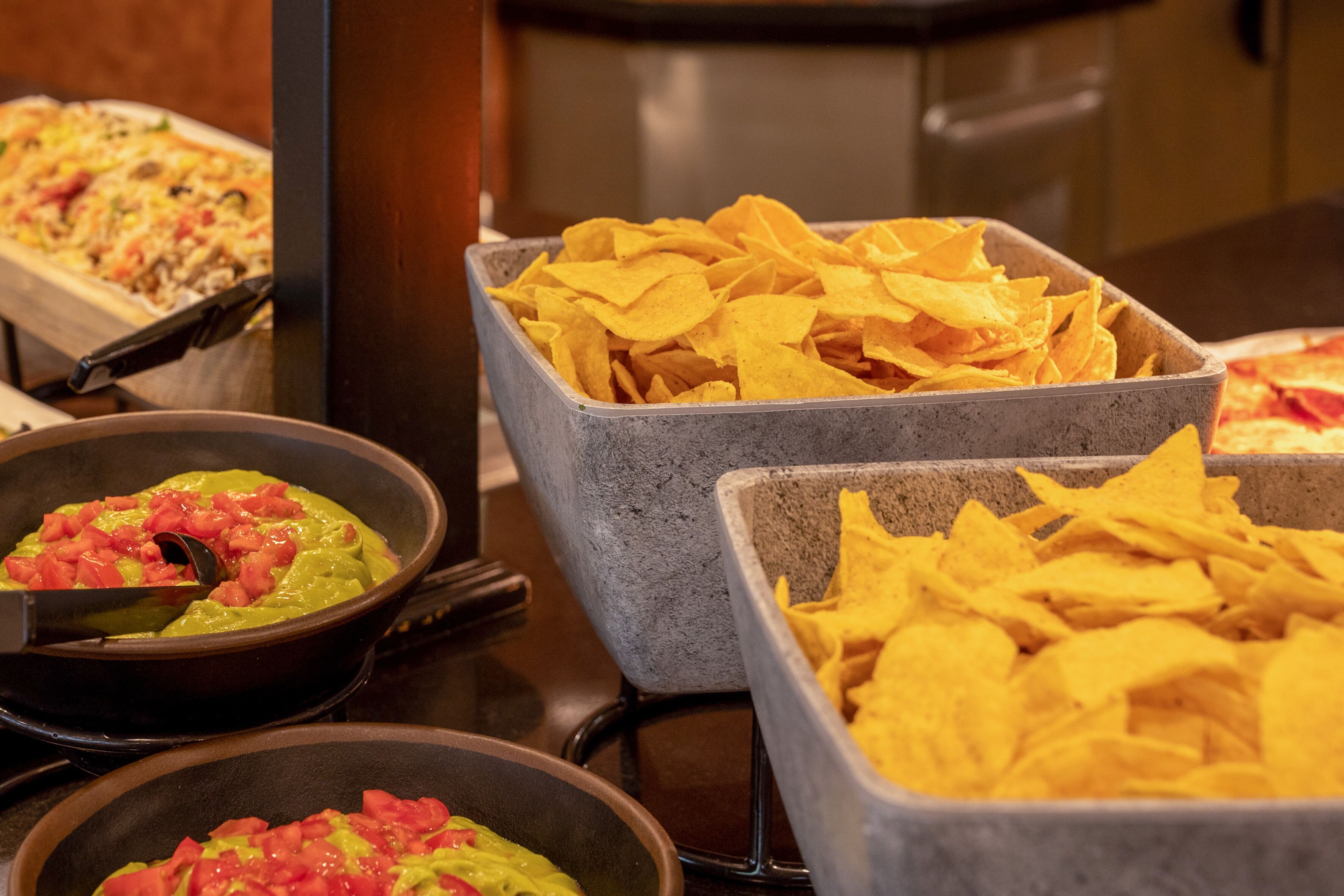 Buffet com nachos, guacamole e um prato com tomates.