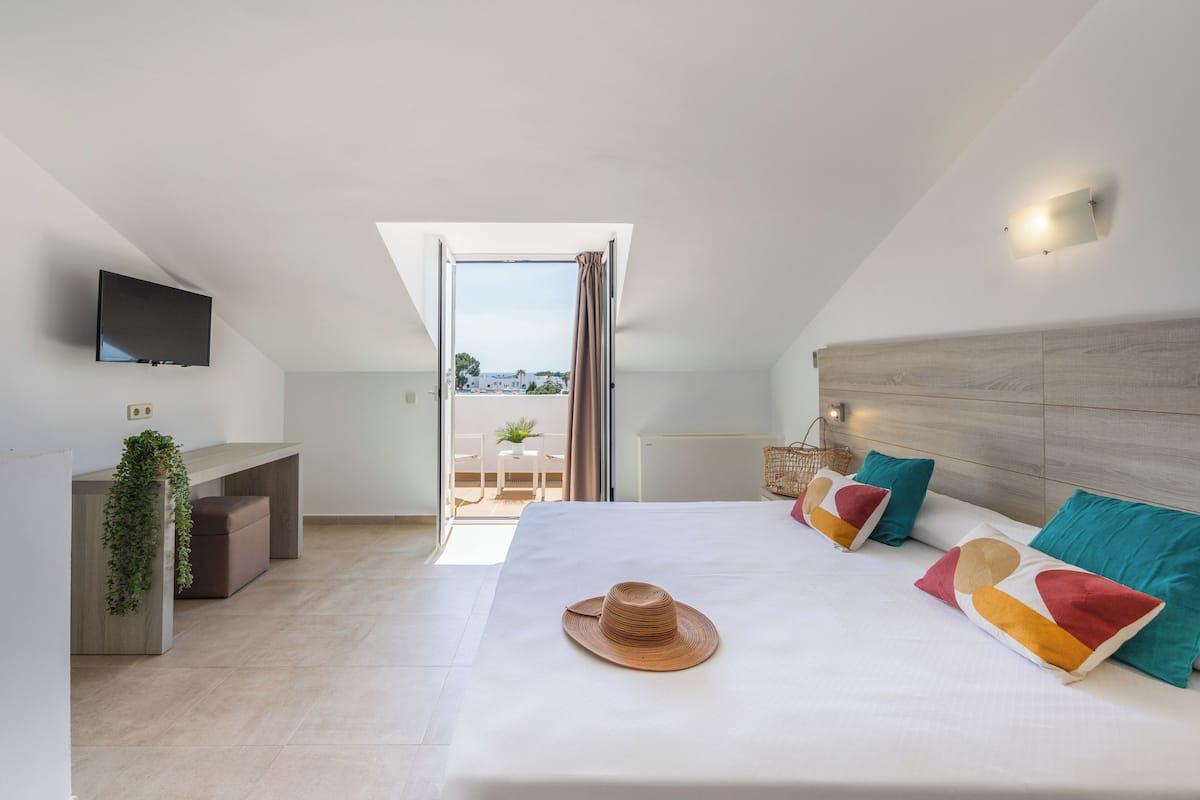 Quarto moderno com uma cama grande, TV fixada na parede e vista para o exterior por uma porta de correr.