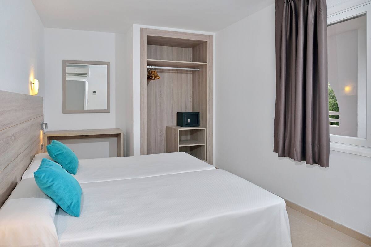 Quarto com cama, guarda-roupa, espelho e janela com cortinas.