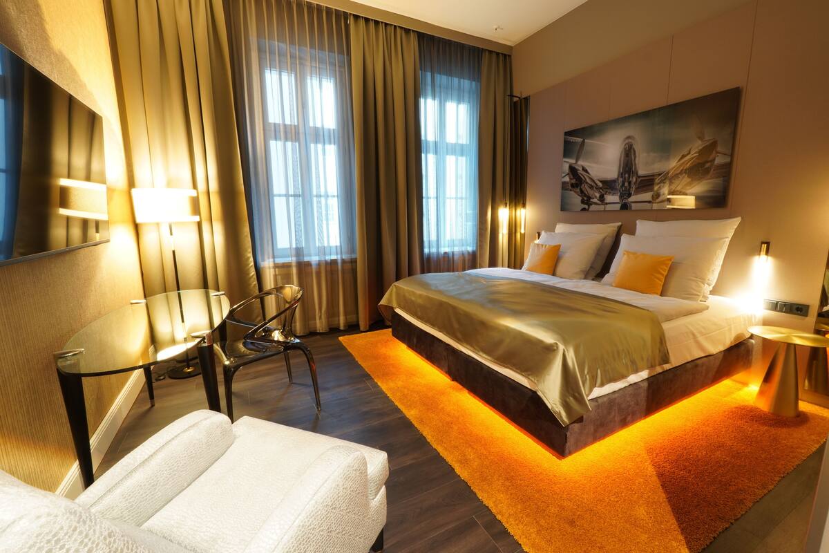 Quarto de hotel com uma cama grande, uma escrivaninha, uma cadeira e um quadro na parede.