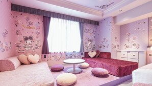 Quarto com decoração em tons de rosa, com cama, sofá, mesa redonda e cômoda.