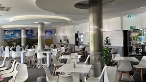 Um restaurante moderno com mesas e cadeiras brancas, piso lustroso e um mural representando uma paisagem de montanhas.