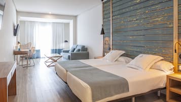 Quarto de hotel moderno com uma cama grande, uma escrivaninha com cadeira, um sofá e vista para o exterior através de uma janela ampla.