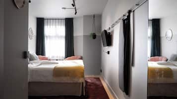 Quarto moderno com duas camas, um espelho grande, ventoinha no teto e televisão fixada na parede.