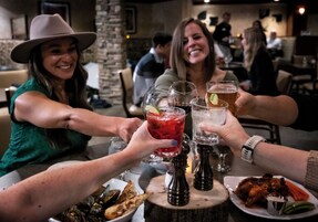 Um grupo de pessoas brindando à mesa de um restaurante, com bebidas e comida.