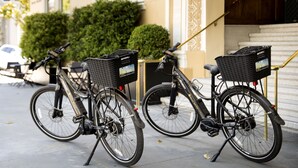 Duas bicicletas estacionadas numa calçada com cestas, em frente a um edifício com o número 2901.