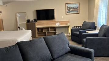 Quarto de hotel com cama, sofá, televisão, escrivaninha e um quadro na parede.