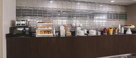 Cozinha moderna com bancada de madeira escura, painel de azulejos e diversos eletrodomésticos e alimentos.