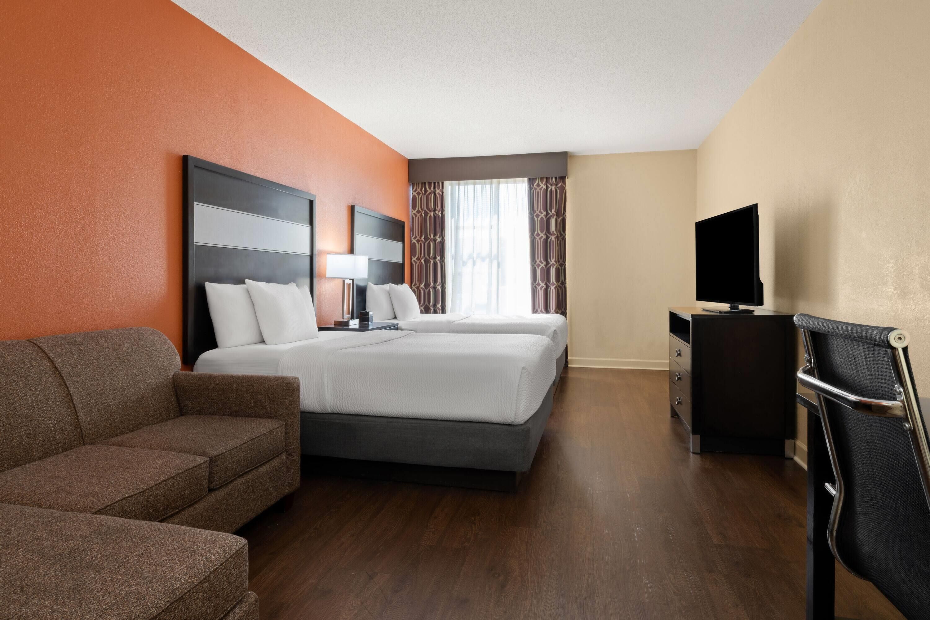 Quarto de hotel com uma cama grande, um sofá, uma TV e uma escrivaninha.