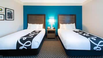 Quarto de hotel com duas camas, uma mesa de cabeceira com abajur e quadros nas paredes.