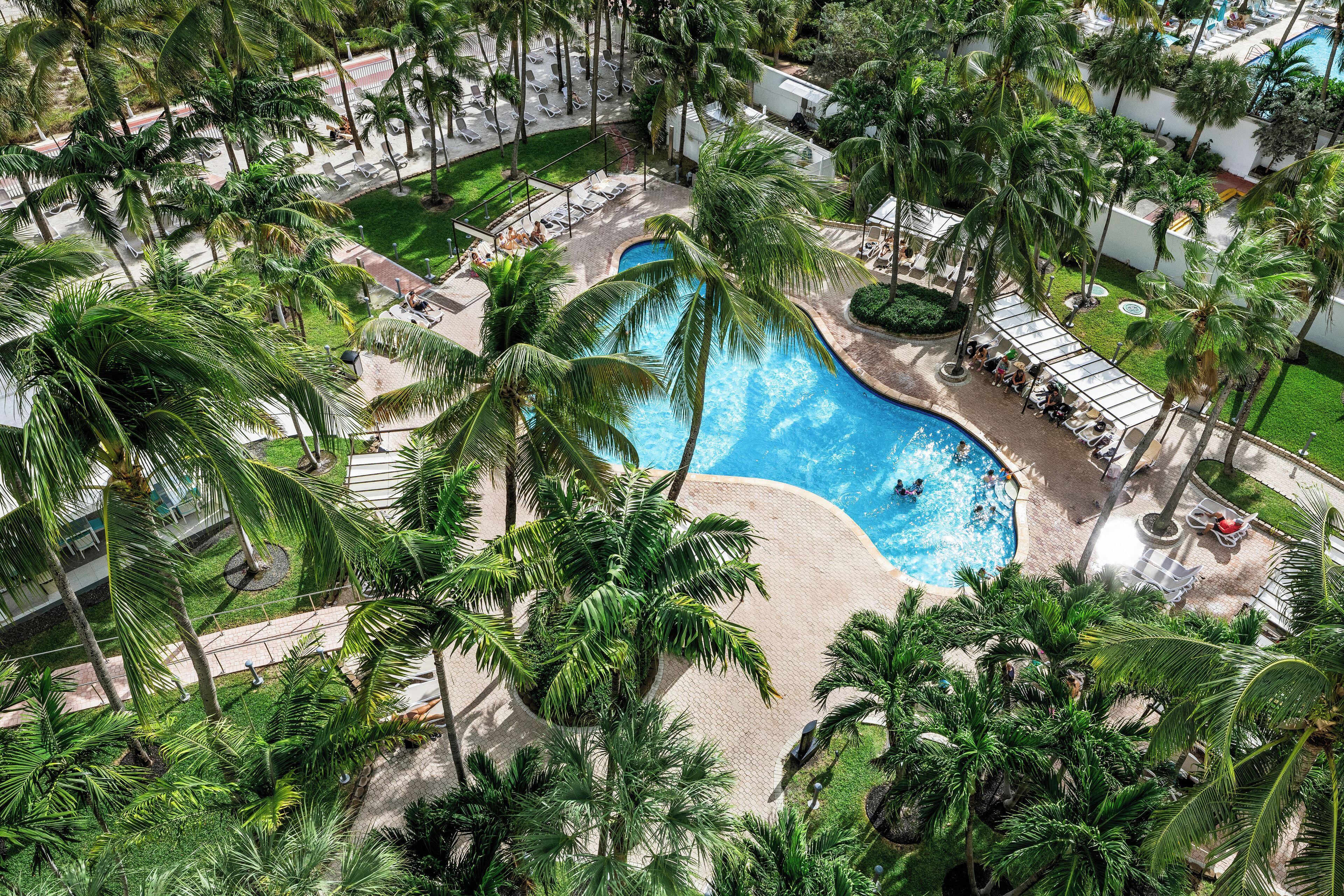 Vista aérea de um resort com piscina central cercada por palmeiras e áreas de descanso.