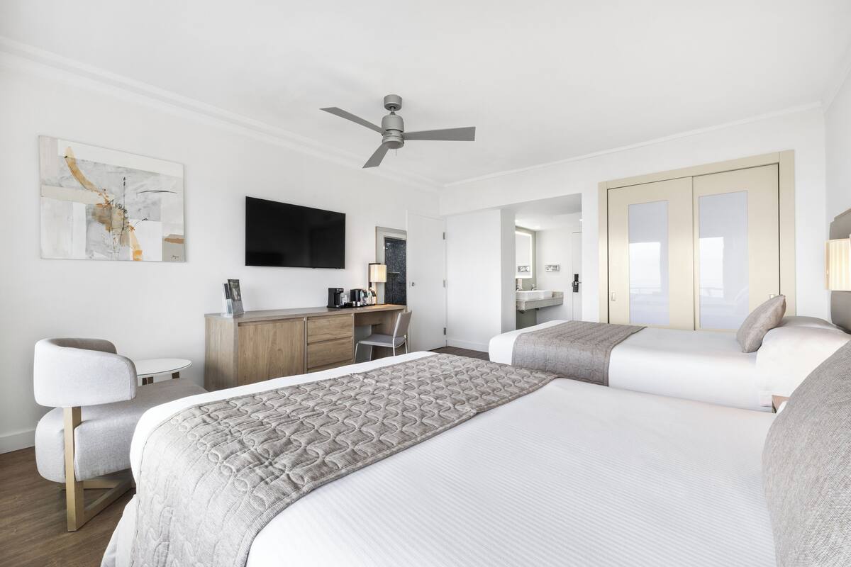 Quarto de hotel moderno com uma cama grande, uma mesa, uma cadeira, uma televisão e um guarda-roupa.