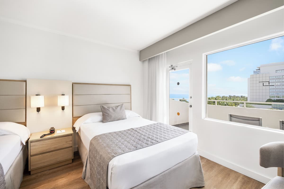 Quarto de hotel com uma janela grande, uma cama, uma mesa de cabeceira com abajur e uma cadeira.