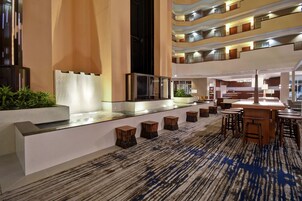 Um saguão de hotel com balcão de recepção, área de estar e escadaria para os andares superiores.