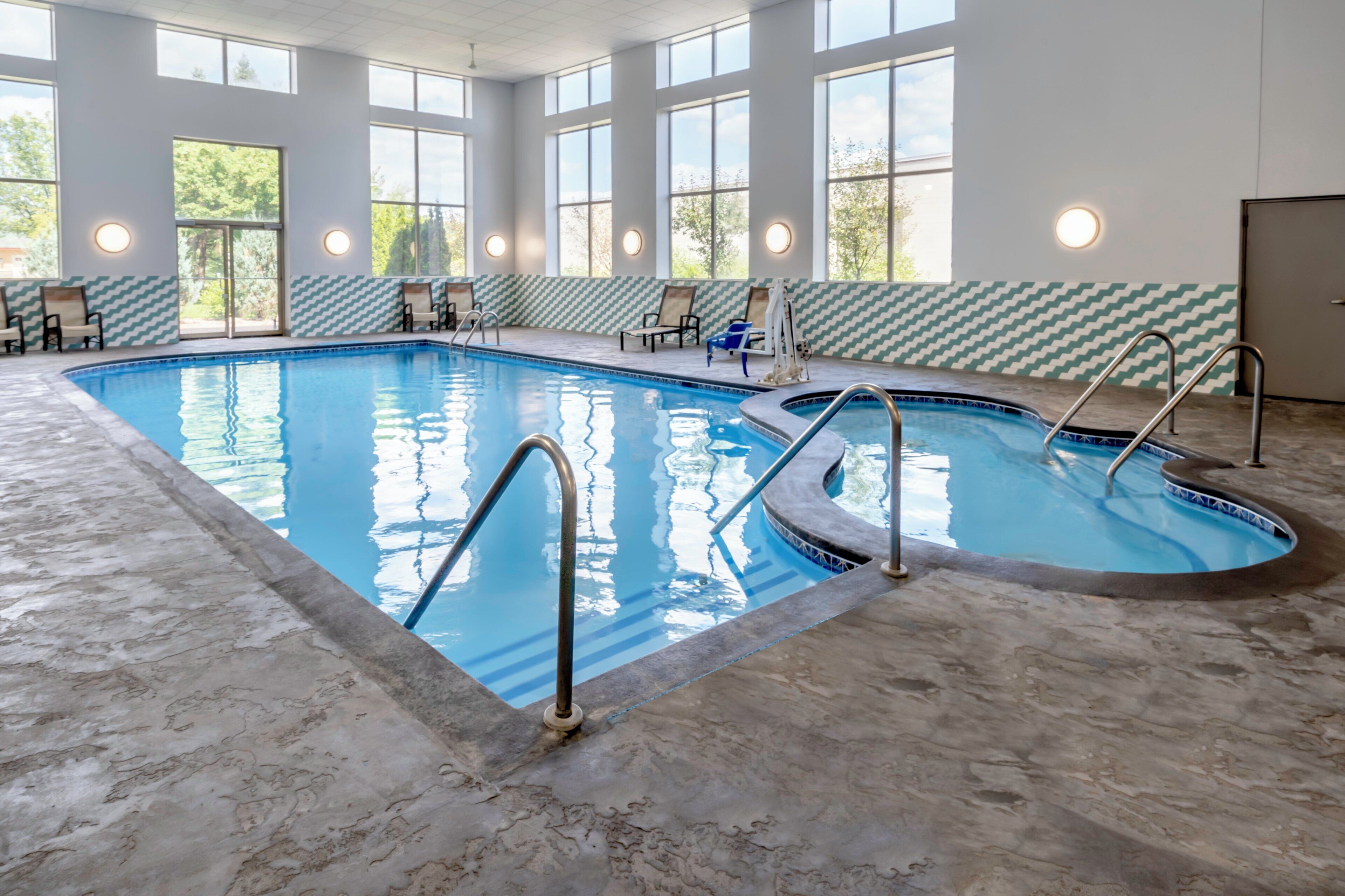 Piscina interna com água cristalina, rodeada por paredes com amplas janelas e um revestimento em padrão herringbone.