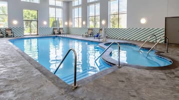 Piscina interna com água cristalina, rodeada por paredes com amplas janelas e um revestimento em padrão herringbone.