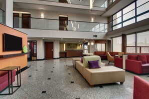Um lobby amplo com teto alto, balcão de recepção, áreas de estar e janelas grandes.