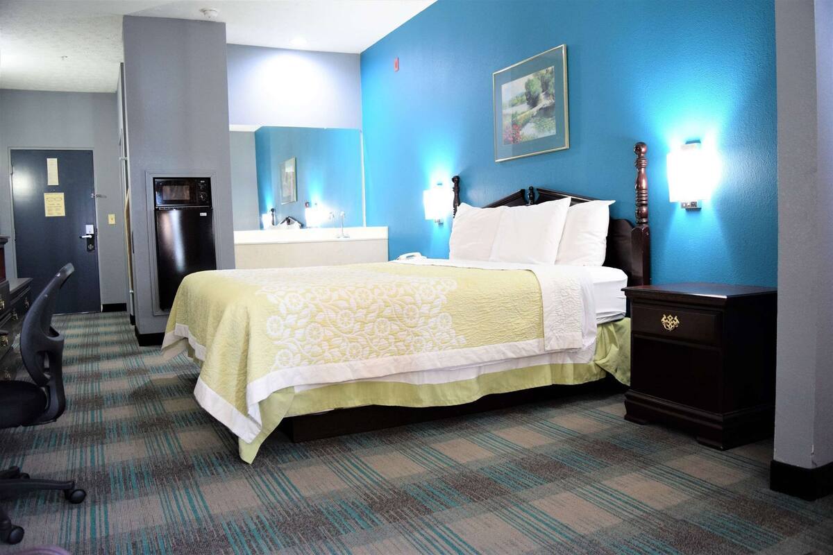 Quarto de hotel com cama, escrivaninha, cadeira, cômoda, espelho e porta.