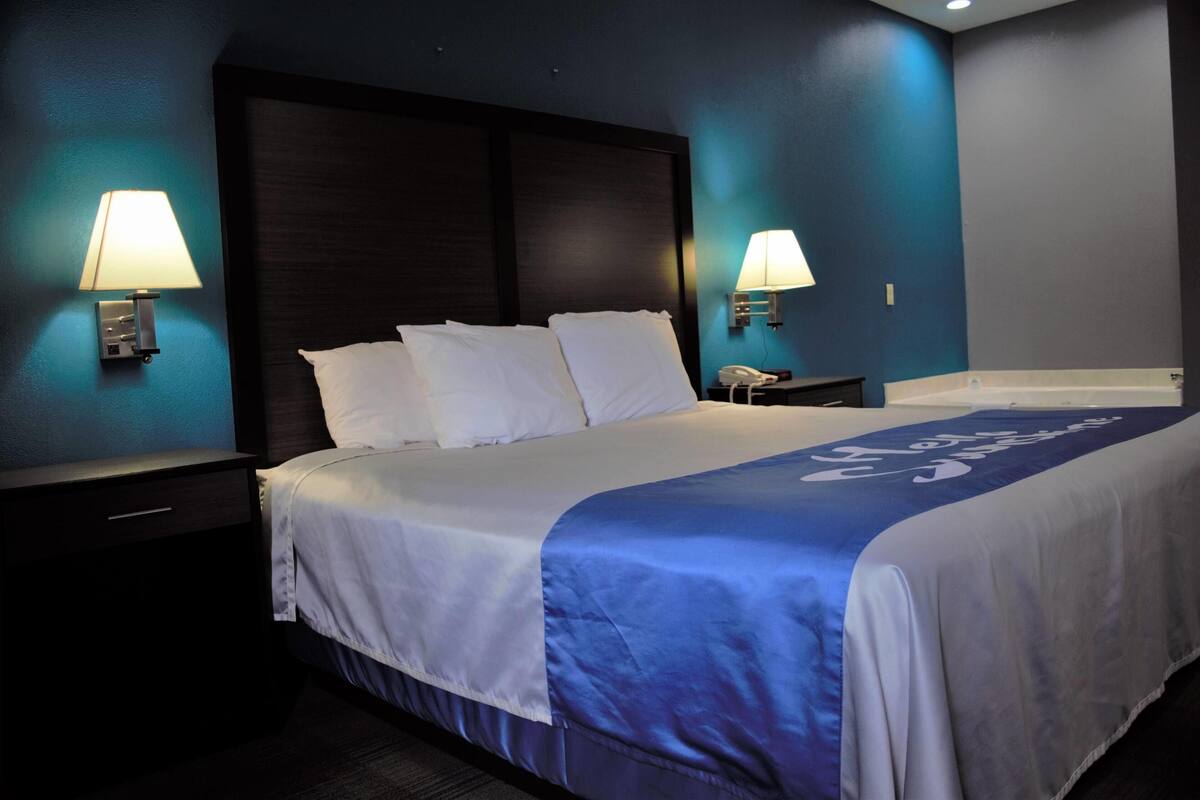 Quarto de hotel com uma cama grande, duas luminárias de cabeceira, uma cabeceira escura e uma parede azul de destaque.