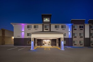 Entrada de hotel moderna com placa, acesso coberto e estacionamento.