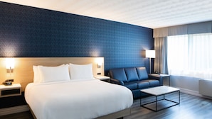 Quarto de hotel moderno com uma cama grande, um sofá, uma mesa de centro e uma mesa de cabeceira com abajur.