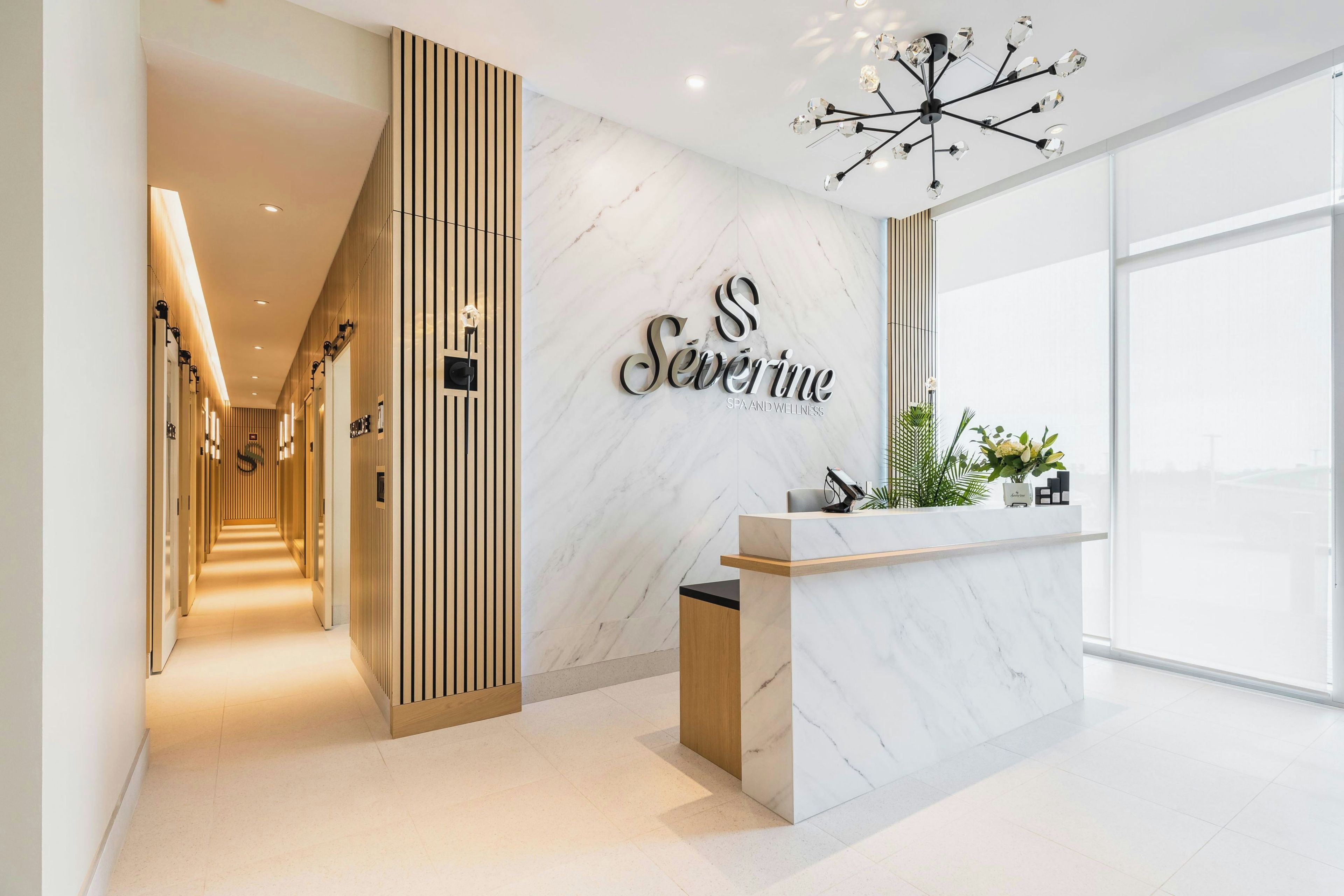 Uma área de recepção moderna com balcão de mármore, uma grande placa fixada na parede e um lustre contemporâneo.