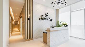Uma área de recepção moderna com balcão de mármore, uma grande placa fixada na parede e um lustre contemporâneo.
