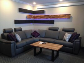 Uma sala de estar moderna com um sofá seccional, uma mesa de centro de madeira e prateleiras embutidas com iluminação azul.