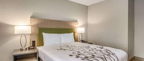 Quarto de hotel com uma cama, duas mesas de cabeceira, luminárias, um painel de cabeceira verde e um cobreleira branca com padrão de galho.