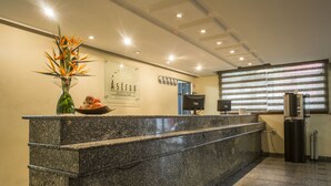 Uma receção com o letreiro 'Astron Hotels & Plazas', um vaso com flores e vista para o átrio.