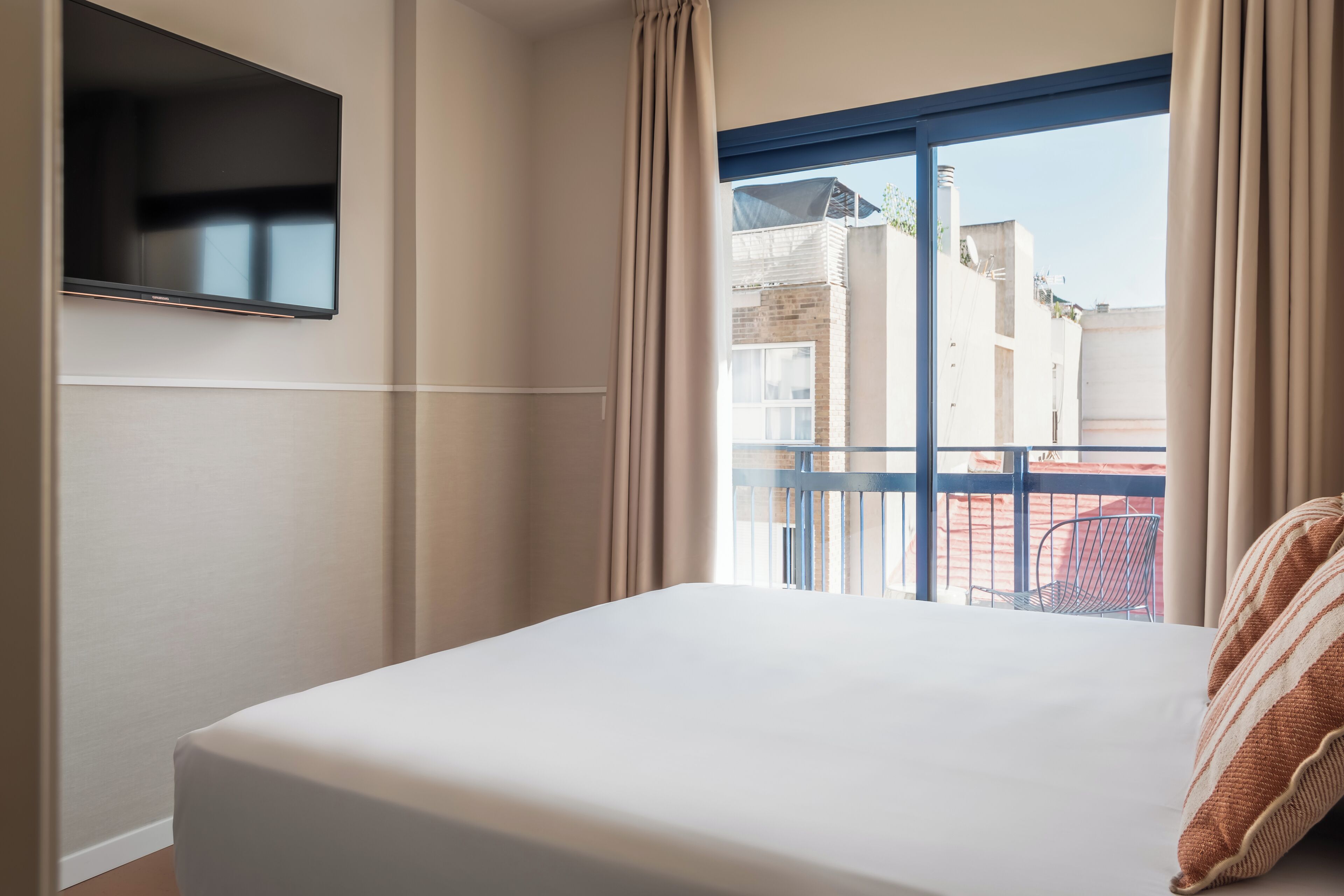Quarto de hotel com cama, televisão na parede e varanda com vista para edifícios.