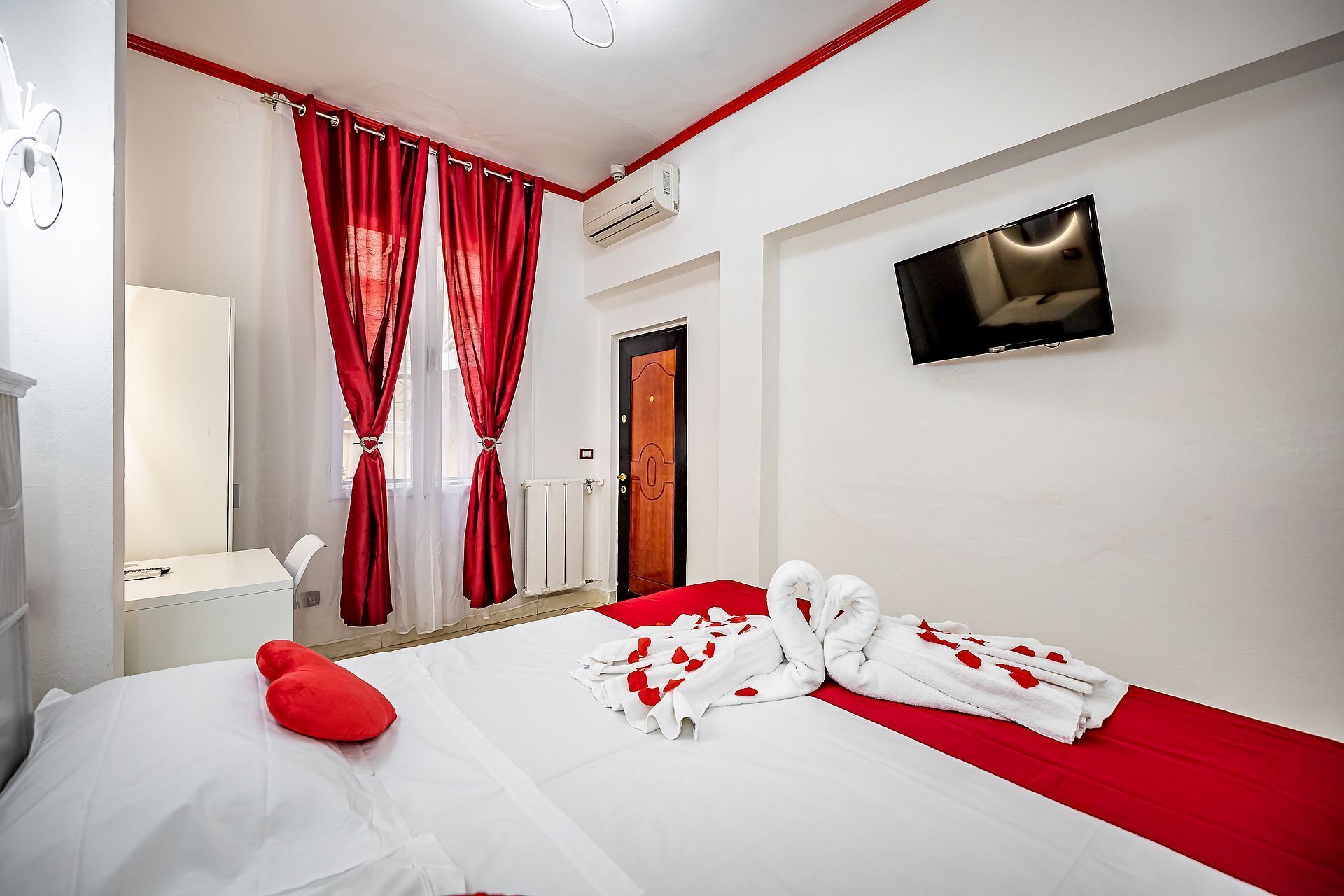 Quarto de hotel com cama, televisão e cortinas vermelhas.