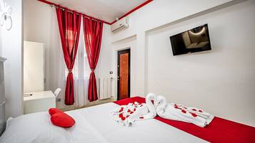 Quarto de hotel com cama, televisão e cortinas vermelhas.