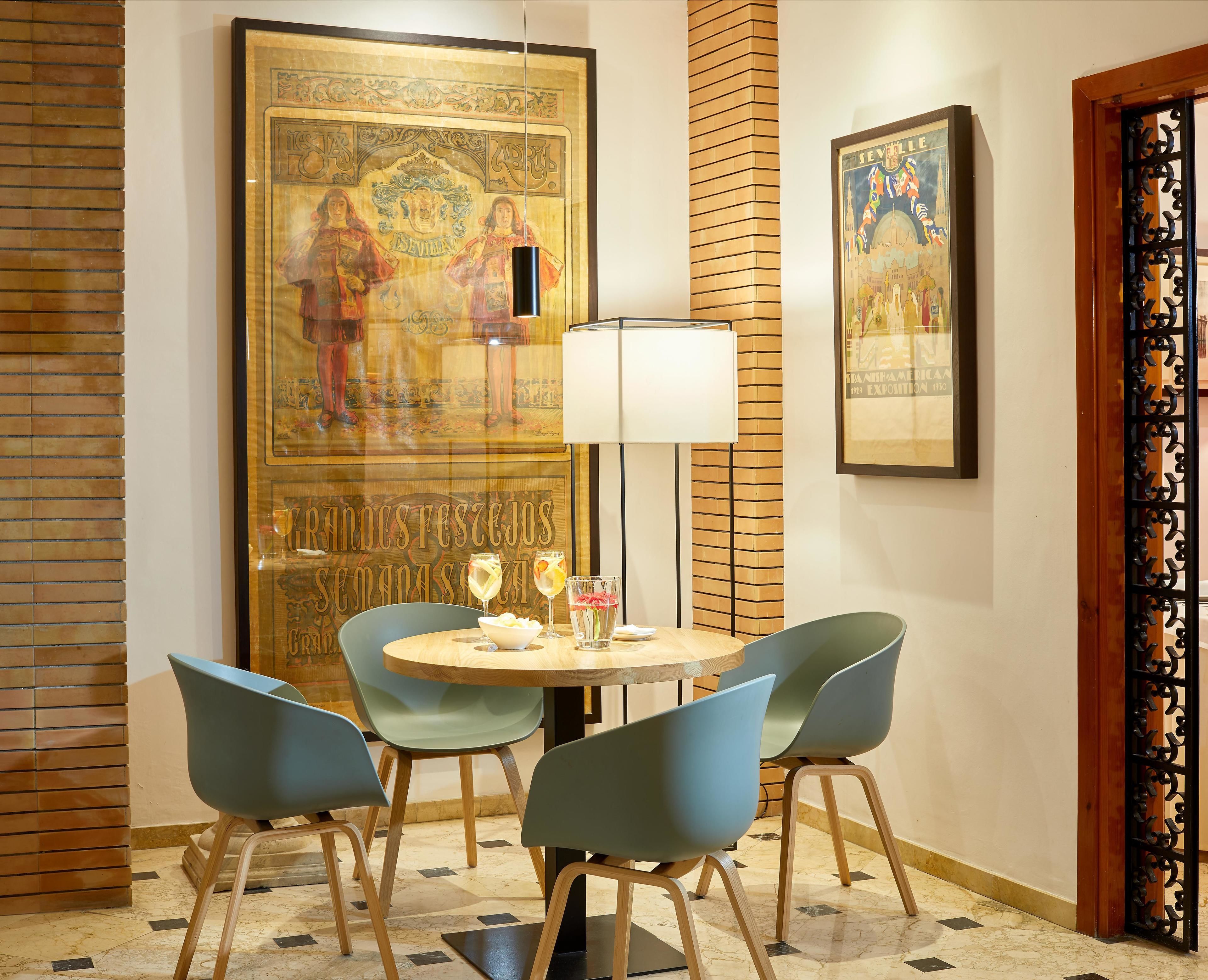 Uma sala de jantar com uma mesa redonda, quatro cadeiras, um abajur e duas obras de arte emolduradas na parede.