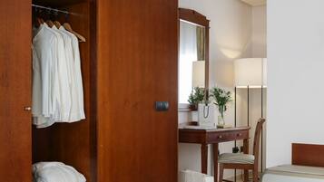 Quarto de hotel com guarda-roupa de madeira, uma mesa com cadeira, uma cama e um espelho.