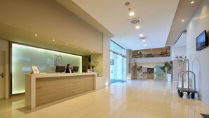 Uma área de recepção de hotel moderna, com um balcão de madeira, uma televisão de tela plana e um chão limpo e reluzente.