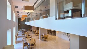 Um amplo hall de hotel com pé direito alto, mobiliário moderno e grandes janelas que permitem a entrada de luz natural.