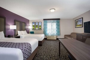 Quarto de hotel com duas camas, uma escrivaninha, televisão e janela com cortinas.