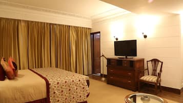 Quarto de hotel com uma cama, televisão, cómoda de madeira, cadeira e uma mesa pequena com tampo de vidro.