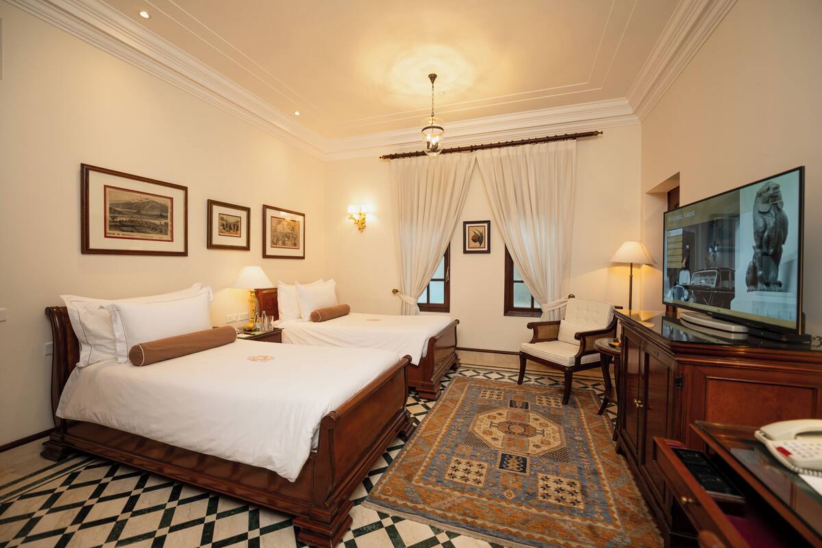 Quarto de hotel com duas camas, televisão, escrivaninha e telefone, além de um tapete estampado.