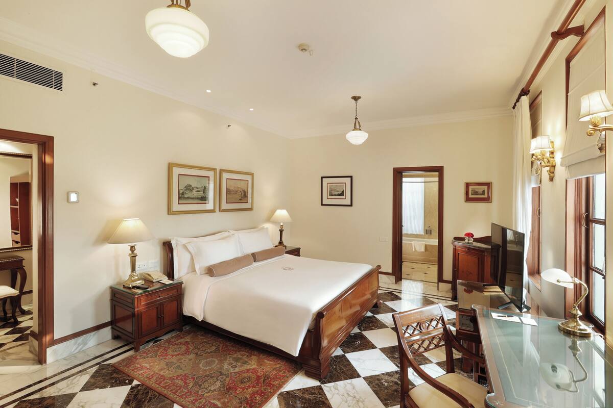 Quarto de hotel com cama, mesas de cabeceira, escrivaninha com cadeira, televisão e um espelho grande.
