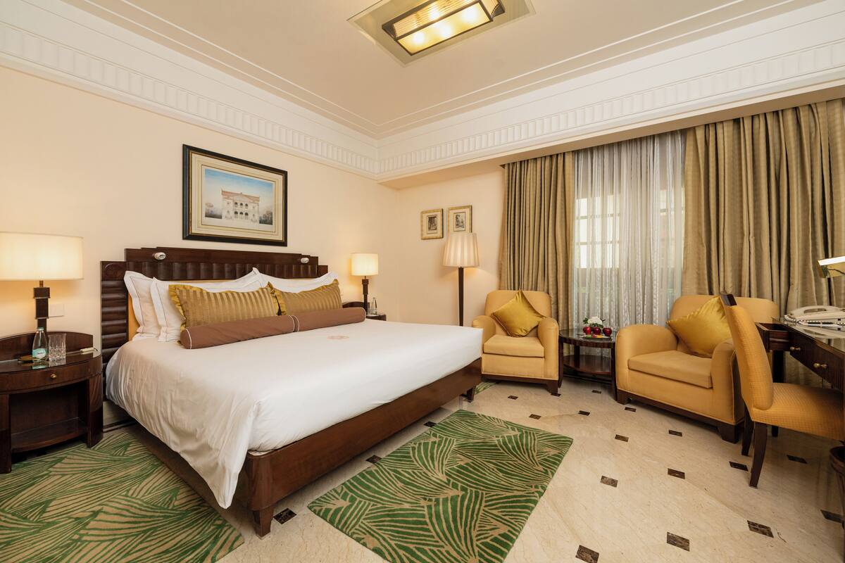 Quarto de hotel com uma cama grande, duas poltronas, uma escrivaninha e uma mesa de cabeceira com abajures.