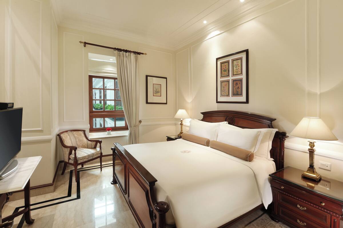 Quarto de hotel com cama grande, mesas de cabeceira, uma cadeira, escrivaninha e televisão.