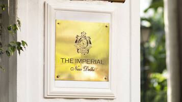 Uma placa numa parede branca com um acessório de latão acima, com a inscrição 'THE IMPERIAL New Delhi'.